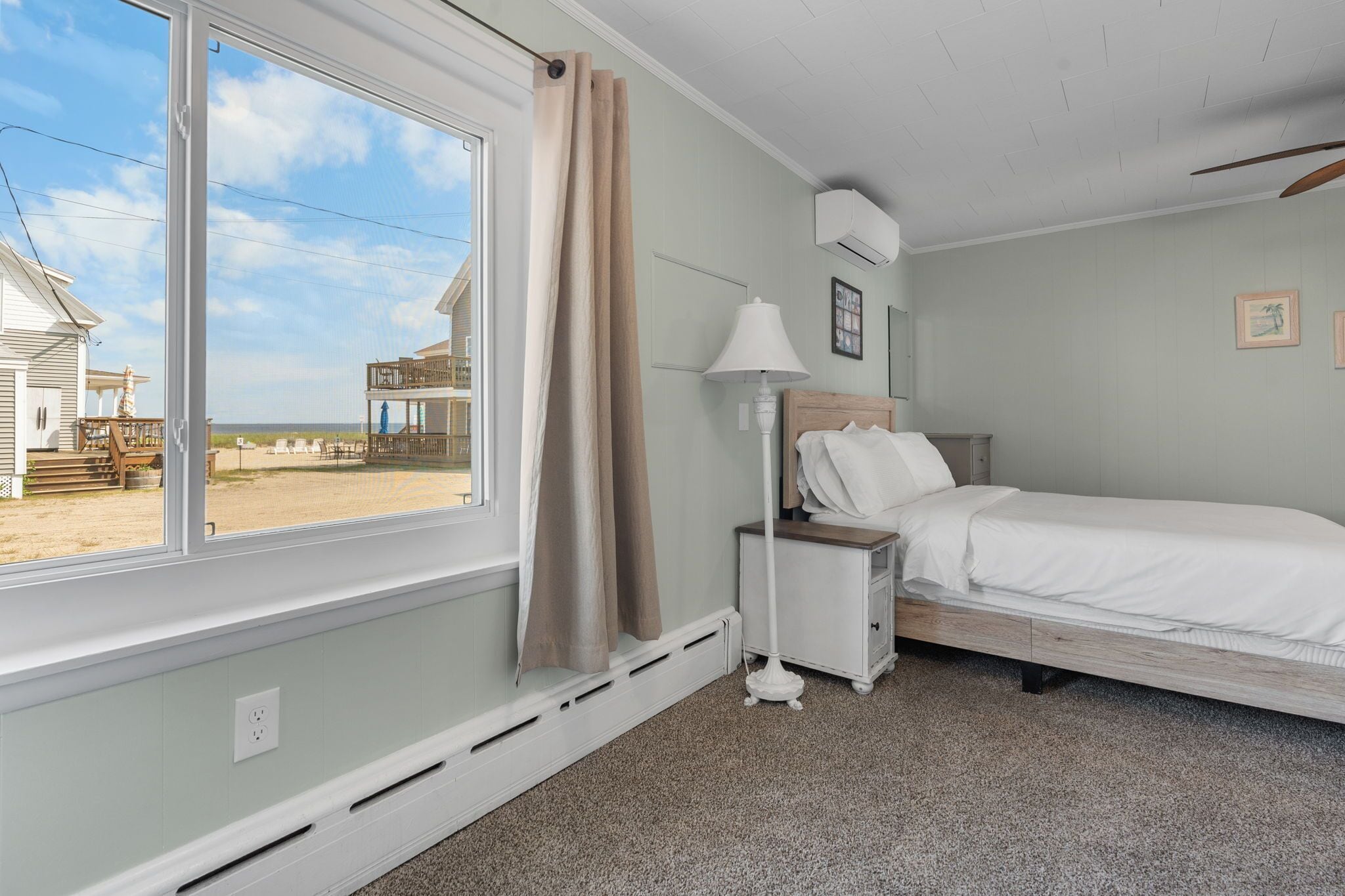 Quarto com cama, mesa de cabeceira, abajur e janela com cortinas.