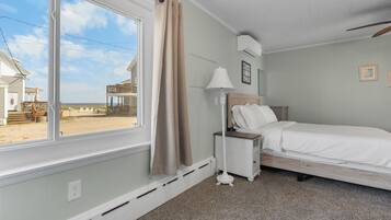 Quarto com cama, mesa de cabeceira, abajur e janela com cortinas.