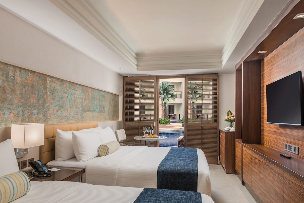 Quarto de hotel com duas camas, televisão, telefone e vista para a piscina e área externa.