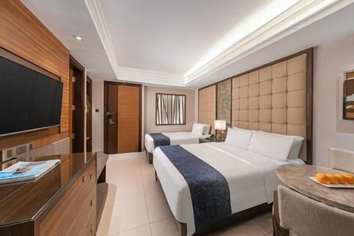 Quarto de hotel com duas camas, televisão, escrivaninha e área de refeições.