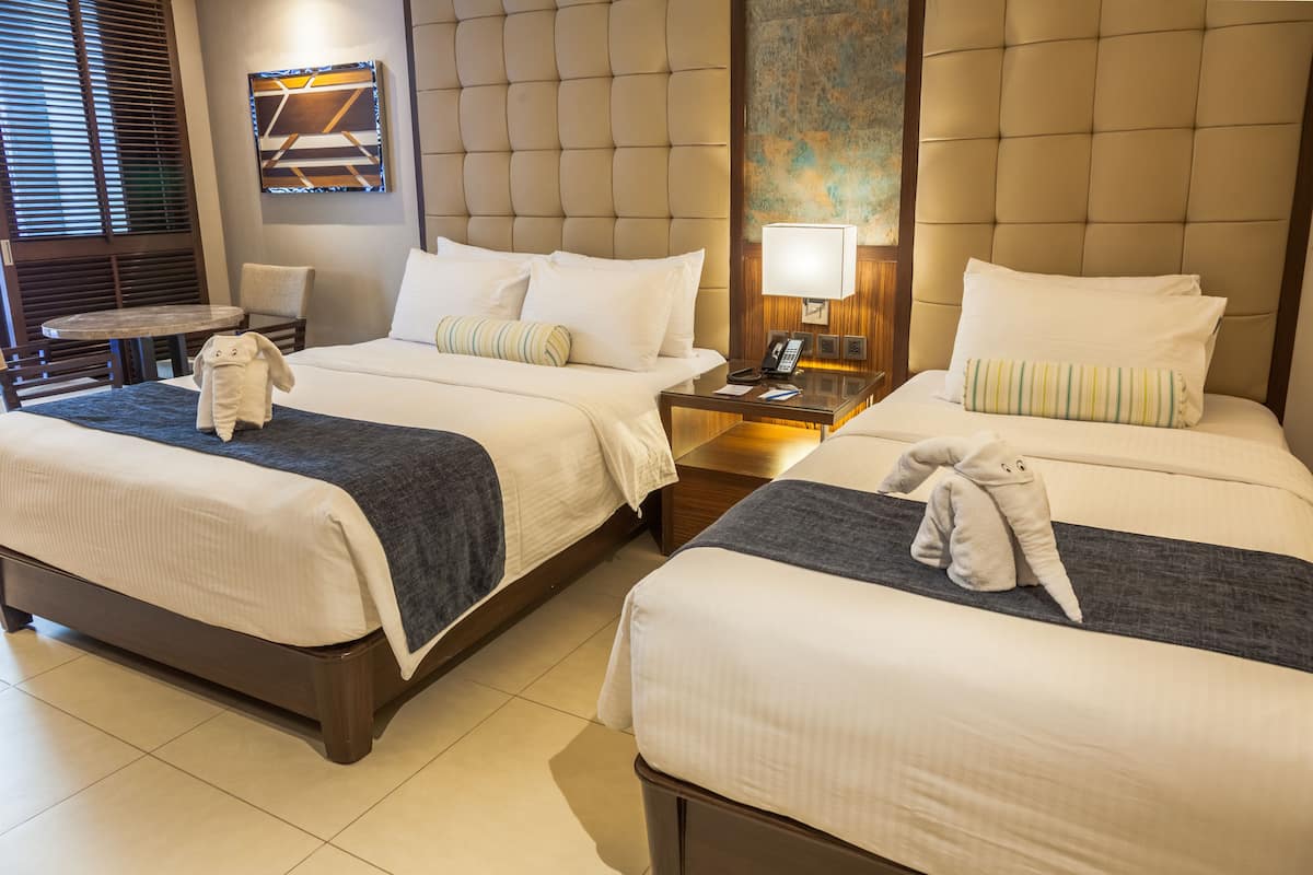 Quarto de hotel com duas camas, uma mesinha e uma luminária.