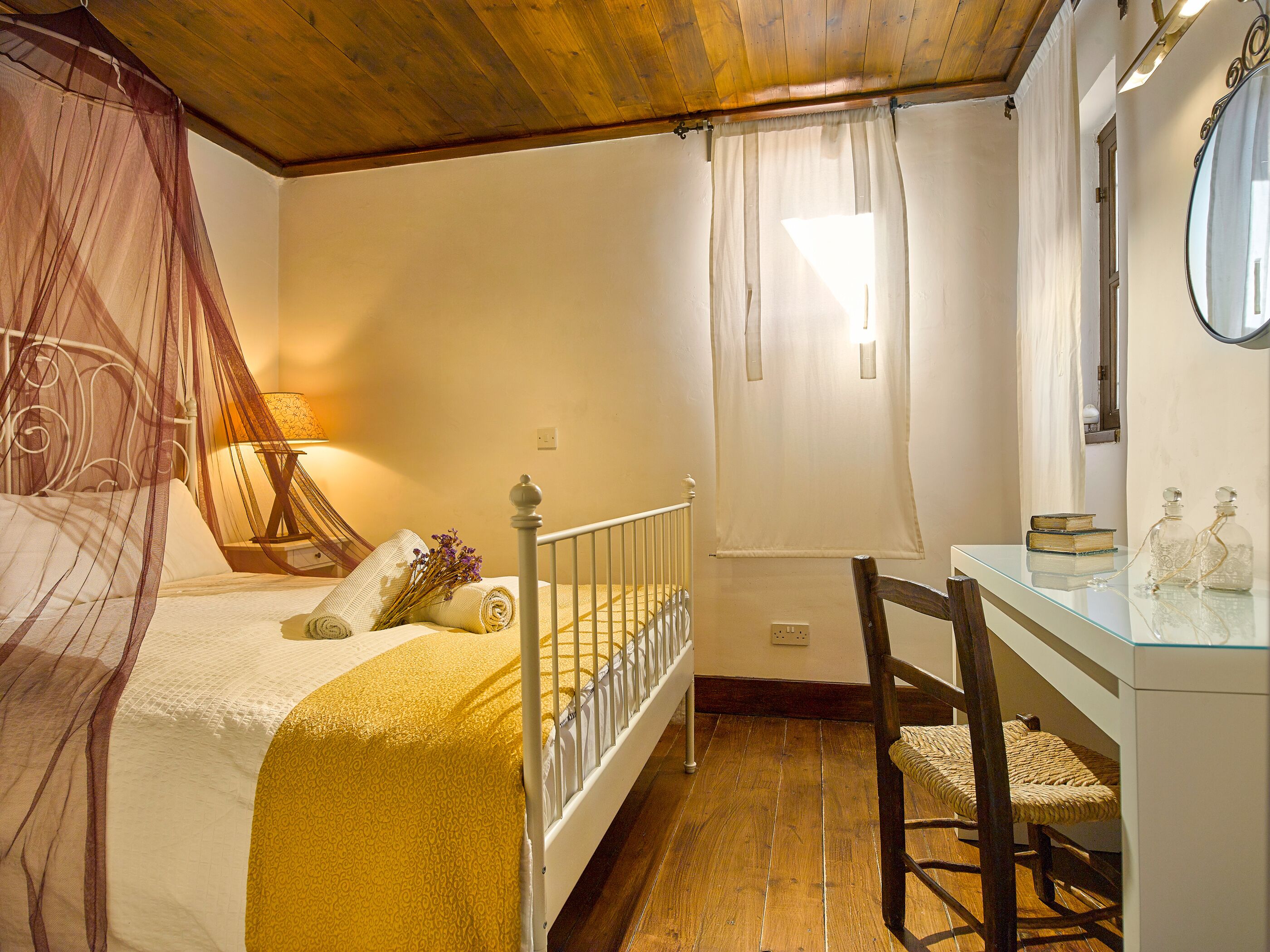 Quarto com cama, escrivaninha, cadeira, mesa de cabeceira, abajur e janela com cortinas.
