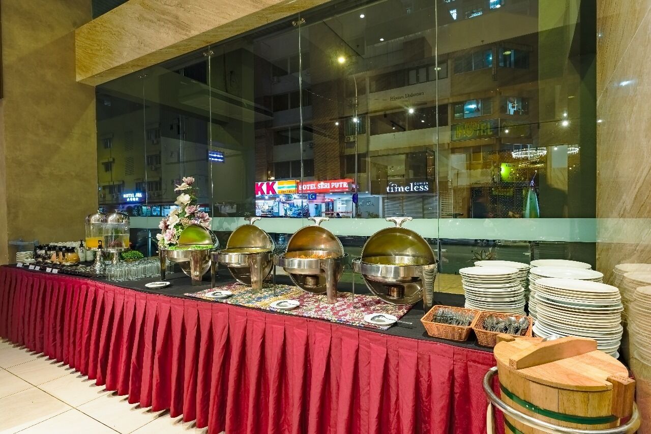 Disposição de buffet com diversas estações de comida, toalha vermelha e vista para um hotel e um edifício com placa.