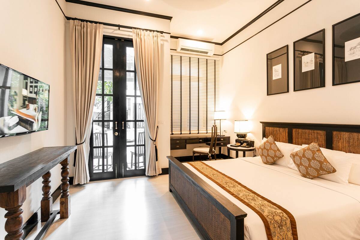 Quarto de hotel com cama grande, escrivaninha, cadeira, televisão e janela com cortinas.