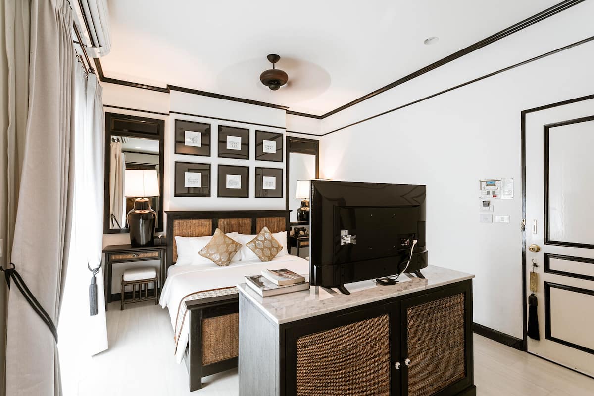 Quarto de hotel com uma cama, mesa de cabeceira, luminária e televisão sobre um móvel.