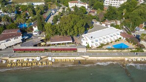 Vista aérea de um hotel à beira-mar, com piscina, área de estar na praia e estacionamento.
