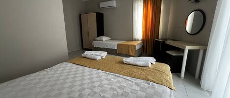 Quarto de hotel com uma cama grande, duas camas menores, uma escrivaninha, um guarda-roupa, um ar condicionado e um espelho.