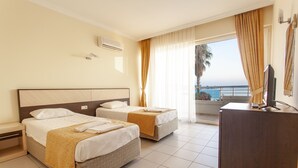 Quarto de hotel com duas camas, televisão e varanda com vista para o mar.