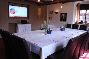 Uma sala de conferências com uma mesa comprida, cadeiras, uma tela de projetor e um quadro na parede.