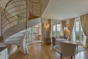 Um interior moderno com escadaria em espiral, sala de estar com sofá e poltronas, e sala de jantar com mesa e cadeiras.