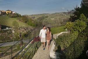 Um casal caminhando em uma escadaria de pedra com corrimão de metal, cercado por vegetação e com vista para uma paisagem montanhosa.