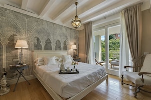 Quarto com cama grande, lustre, mesa de cabeceira e vista para o exterior.