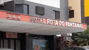 Exterior do Hotel Rota do Pantanal, com um grande mural de papagaio e dois carros estacionados em frente.