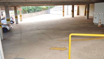 Uma garagem de estacionamento com um carro branco estacionado sob um pilar de concreto. Uma seta amarela no chão indica a direção.