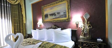 Quarto de hotel com cama, um quadro, um relógio e uma estátua em uma mesinha de cabeceira.
