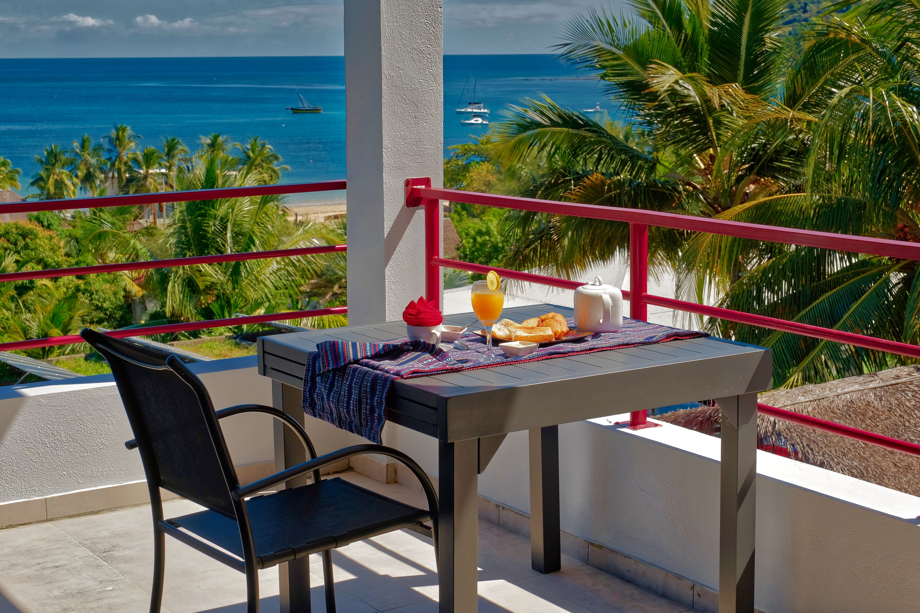 Varanda com mesa posta para o café da manhã, com vista para a praia e o oceano.