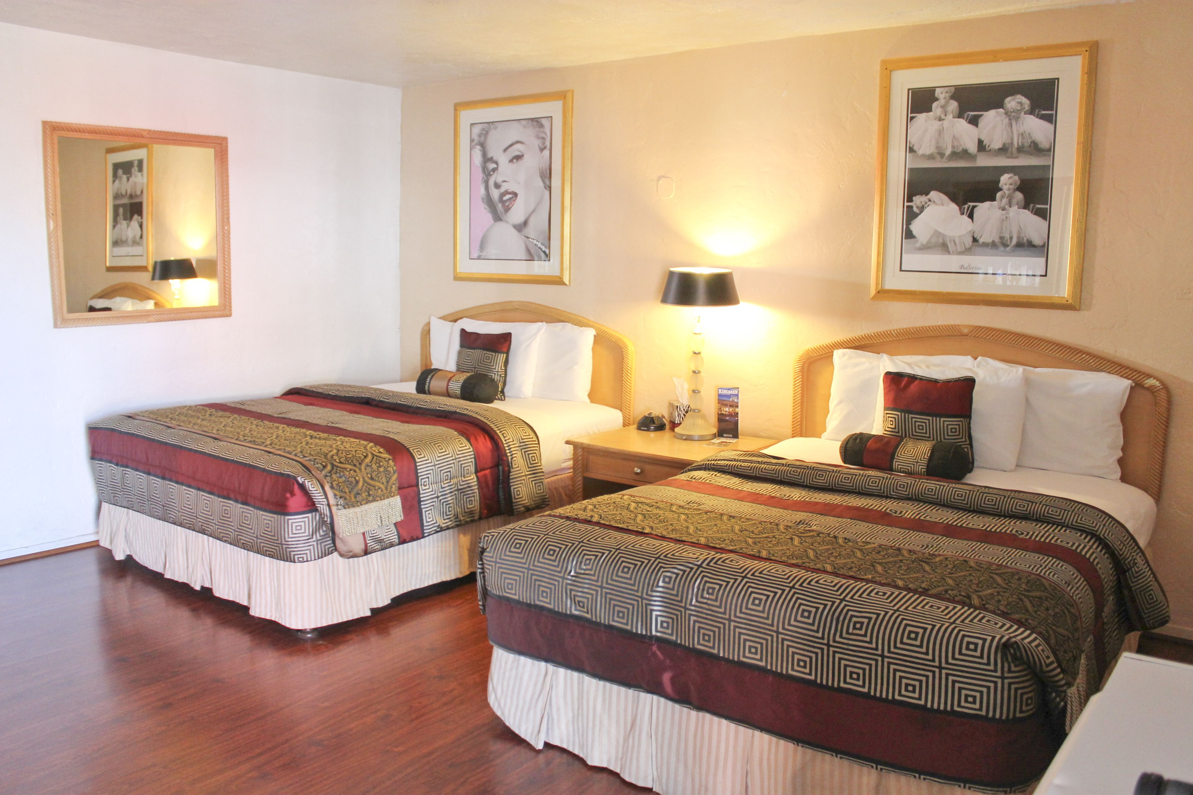 Quarto de hotel com duas camas, cada uma com roupa de cama estampada, uma mesinha de cabeceira com abajur e quadros nas paredes.