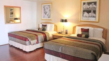 Quarto de hotel com duas camas, cada uma com roupa de cama estampada, uma mesinha de cabeceira com abajur e quadros nas paredes.