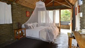 Quarto com cama sob uma rede mosquiteira, mesa de cabeceira de madeira e parede de pedra.