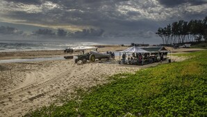 Uma praia com uma área coberta por tendas, um trator e uma carreta.
