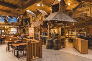 Restaurante de temática rústica com mobiliário de madeira, área de bar e um mural na parede.