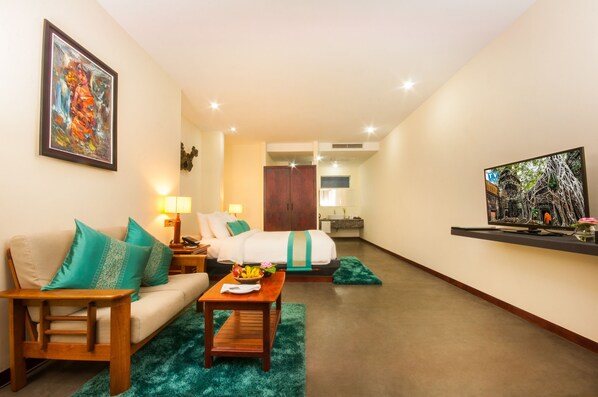Quarto de hotel com sofá, cama, TV e banheiro visível ao fundo.