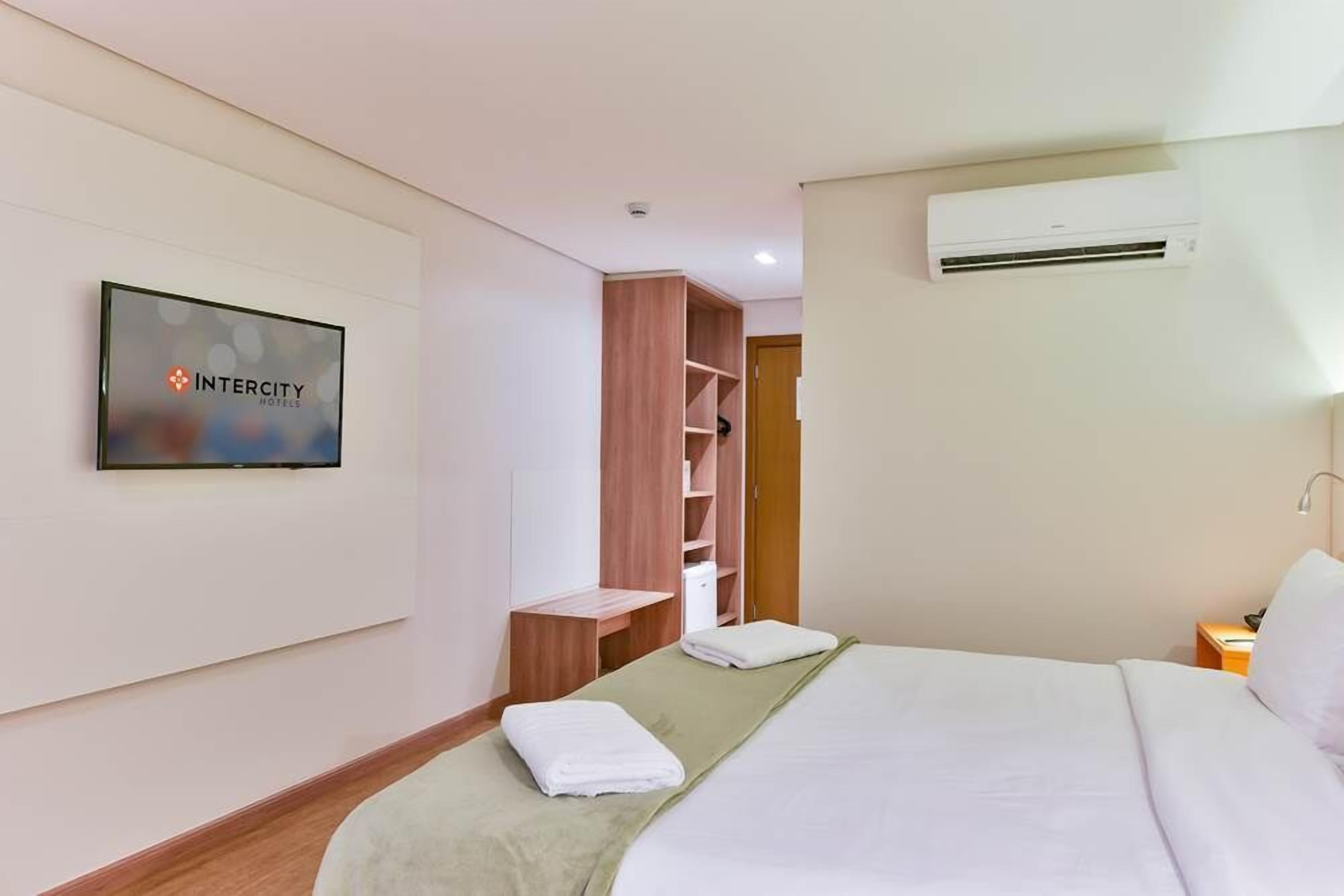 Quarto de hotel com cama, televisão na parede, guarda-roupa e ar condicionado.