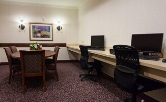 Uma sala de conferências com uma mesa redonda, quatro cadeiras, dois computadores e um quadro na parede.
