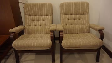 Duas poltronas estofadas com padrão listrado, posicionadas em frente a uma parede com chão de madeira e tomadas elétricas brancas.