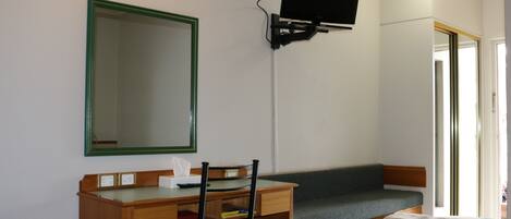 Quarto com cama, escrivaninha com cadeira, televisão na parede e espelho.