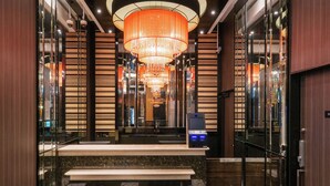 Um hall de hotel moderno com uma recepção de mármore, um candelabro grande e um quiosque de check-in digital.
