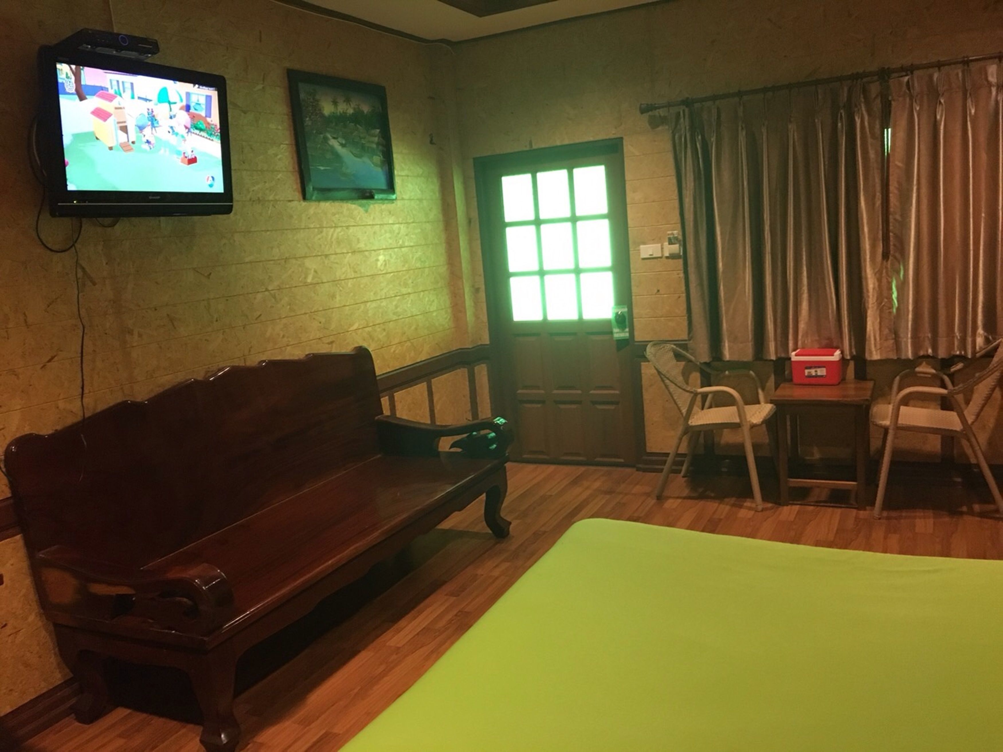 Quarto com um banco de madeira, uma cama, uma mesa com cadeiras, uma televisão e uma janela com cortinas.