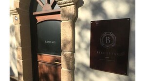 Uma porta com a inscrição 'ROOMS' e uma placa com 'BIENESTAR' e um 'B' com monograma.