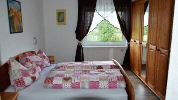 Quarto com cama de madeira, janela com cortinas, guarda-roupa e um quadro na parede.