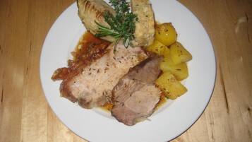 Prato com carne fatiada, batatas assadas e um ramo de ervas.