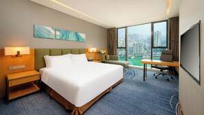 Quarto de hotel com cama grande, escrivaninha, cadeira, televisão e vista para a cidade.