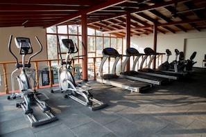 Uma academia com diversos equipamentos de cardio, incluindo elípticos e esteiras, sob um teto de madeira com grandes janelas.