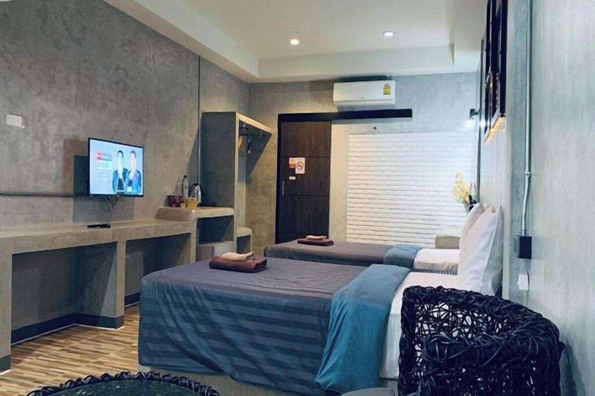 Quarto de hotel moderno com duas camas, televisão, secretária e uma janela grande.
