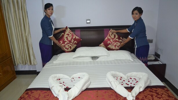 Cama bem arrumada com toalhas em formato de coração e almofadas decorativas.