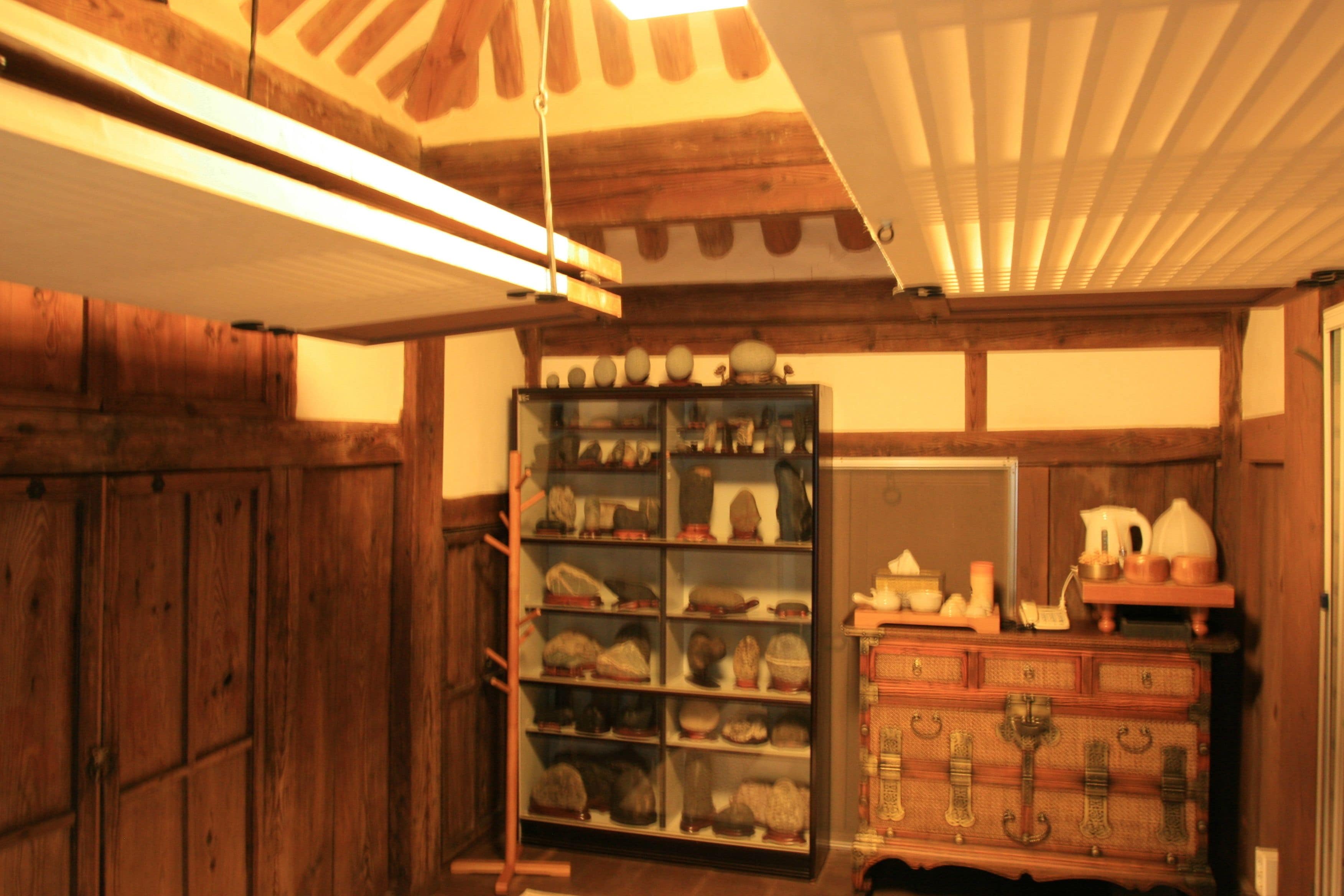 Quarto com paredes de madeira, uma vitrine de vidro com diversos objetos e um aparador antigo.