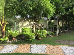 Um jardim com diversas plantas, uma palmeira e uma cerca de madeira.