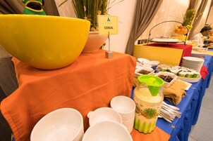Mesa de buffet com um recipiente amarelo, uma placa com a inscrição 'Cereal' e diversas opções de comida.