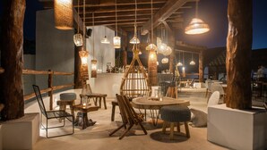 Área externa com assentos de madeira rústica, luminárias de vime pendentes e um bar com garrafas.