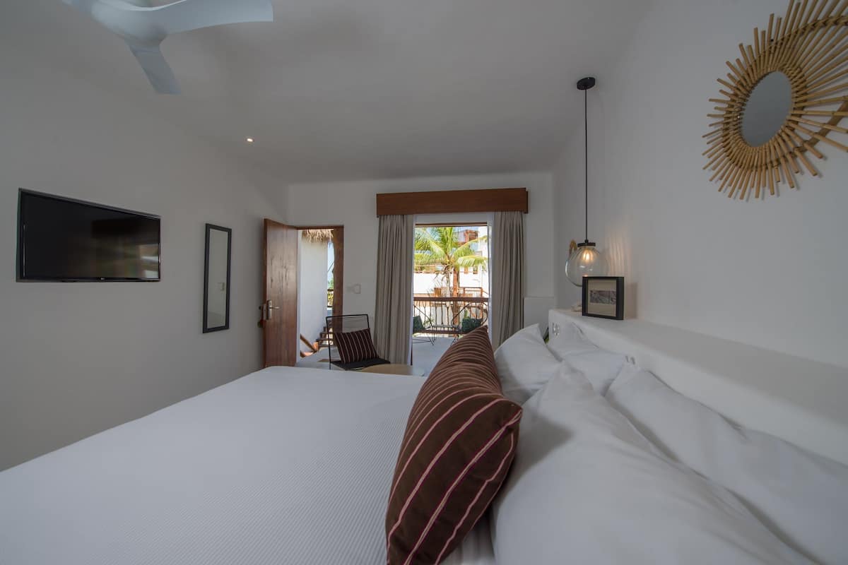 Quarto de hotel com uma cama grande, televisão na parede, luz no teto e vista para a varanda.