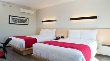 Quarto de hotel com duas camas, uma escrivaninha, uma cadeira e um aparelho de ar condicionado.