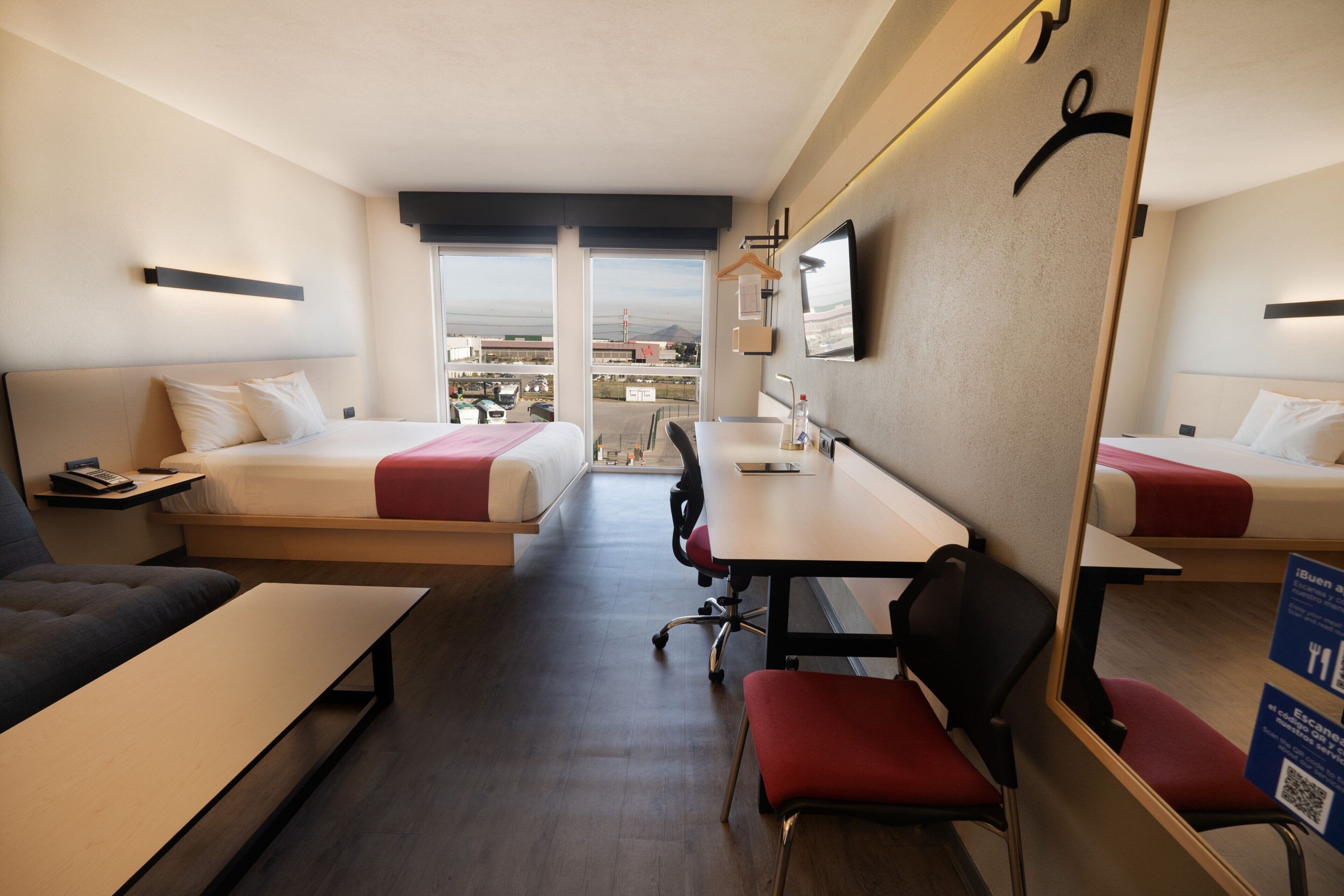 Quarto de hotel com duas camas, uma escrivaninha, uma cadeira e um espelho grande.