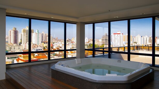 Quarto moderno com amplas janelas com vista para a cidade, piso de madeira e banheira de hidromassagem.