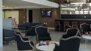 Um hall moderno com parede de madeira, cadeiras estofadas pretas, mesa de centro branca e luminárias pendentes.