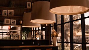 Uma área de bar com luminárias pendentes, prateleiras com quadros emoldurados e vista para carros estacionados lá fora.