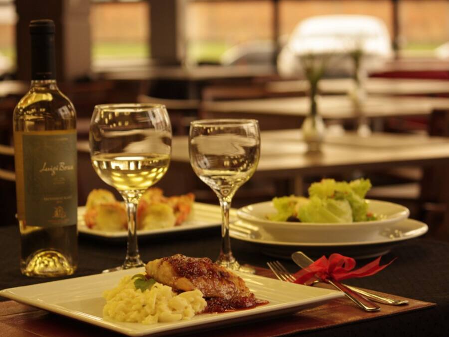 Uma mesa de jantar com uma garrafa de vinho, duas taças de vinho, um prato com comida e um guardanapo vermelho.